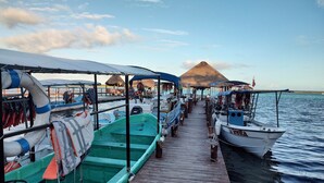 Um cais com barcos atracados, uma construção com telhado de palha e um mar calmo.