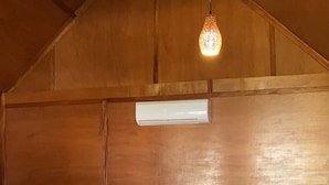 Quarto com painéis de madeira, cama, almofadas, mesa de cabeceira e luminária suspensa.