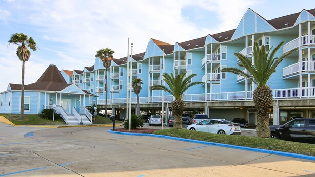 Um hotel de vários andares com varandas, palmeiras e estacionamento.