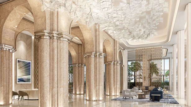 Um lobby amplo com tetos altos, grandes colunas e um lustre moderno. Há áreas de estar e uma grande obra de arte na parede.