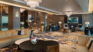 Um hall de hotel moderno com um sofá grande, uma mesa de centro redonda e um lustre.