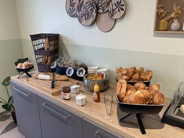 Buffet de café da manhã com pães, bolos e acompanhamentos.
