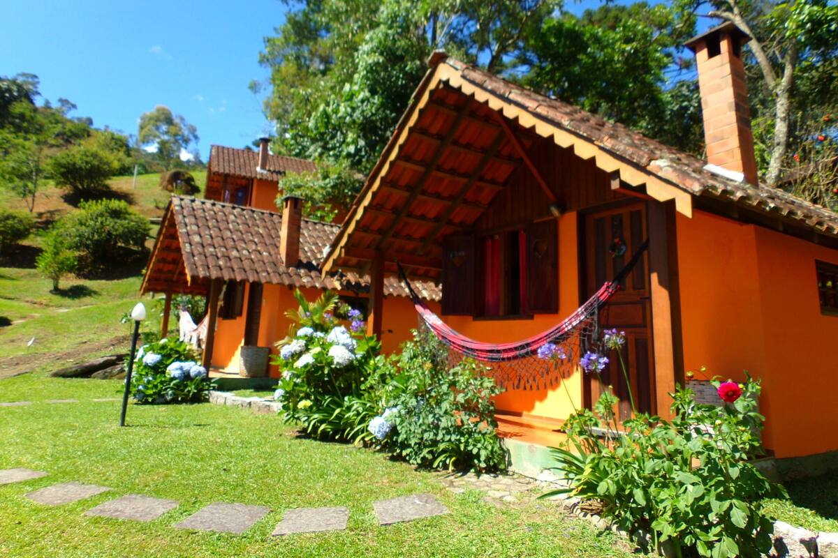 Uma casa rústica com telhado de telhas, uma chaminé e uma rede na varanda da frente.