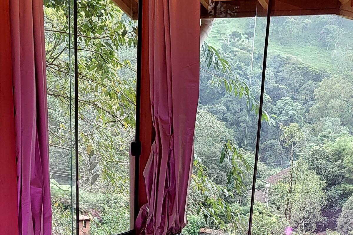 Um quarto de spa com uma banheira grande, teto de madeira e vista para uma paisagem exuberante através de amplas janelas.