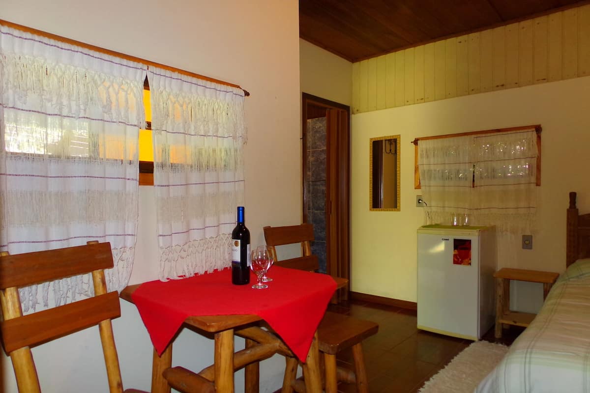 Uma área de refeições com mesa e cadeiras de madeira, uma garrafa de vinho e dois copos de vinho.
