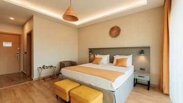 Quarto de hotel moderno com uma cama grande, uma mesinha de cabeceira, uma cadeira, um candeeiro pendente e chão de madeira.