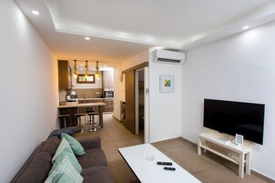 Uma sala de estar moderna com sofá, mesa de centro e televisão sobre um suporte.
