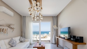 Uma sala de estar moderna com sofá, mesa de centro e televisão. Uma grande janela oferece vista para a praia.