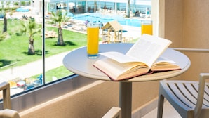 Varanda com vista para o oceano, uma mesa com um livro e um copo de suco de laranja, e uma cadeira.