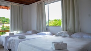 Quarto de hotel com duas camas, roupa de cama branca e vista para o verde lá fora.
