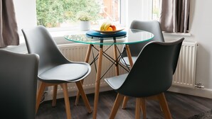 Uma sala de jantar moderna com uma mesa de vidro redonda, duas cadeiras cinzentas e um vaso de planta.