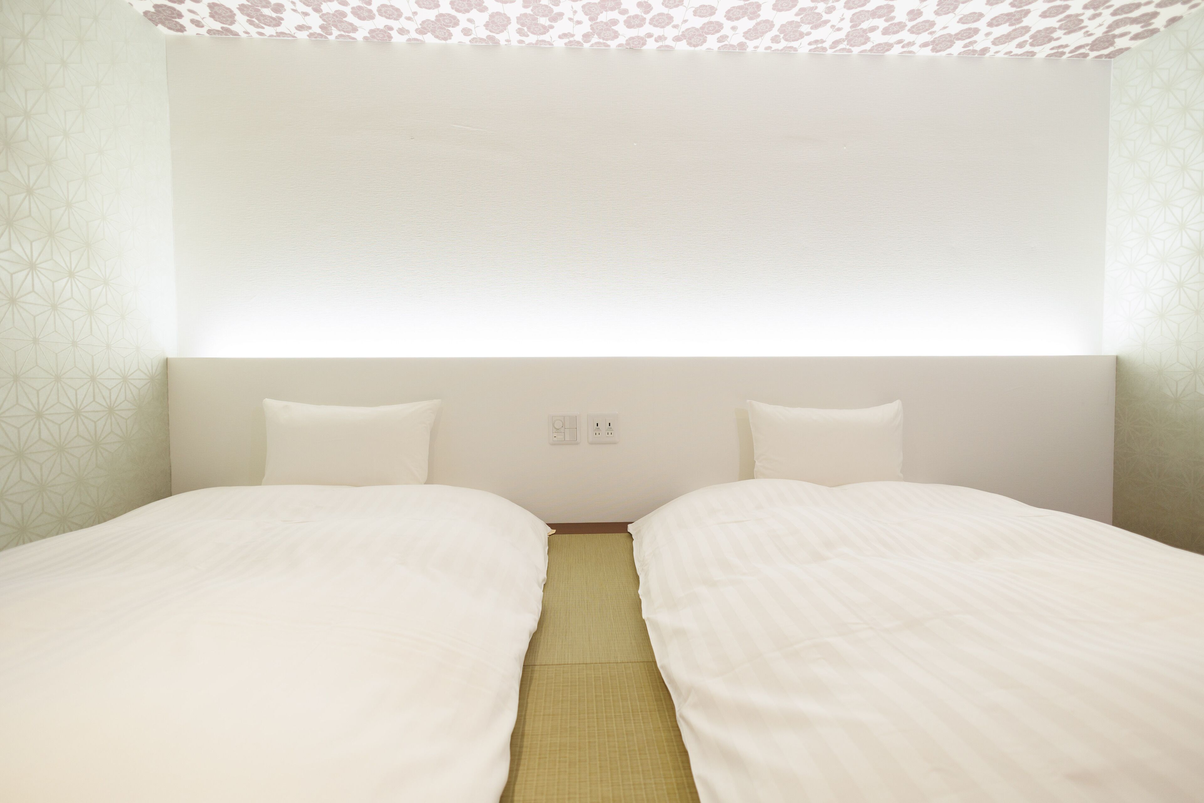 Quarto de hotel com duas camas, uma cabeceira simples e um papel de parede estampado.