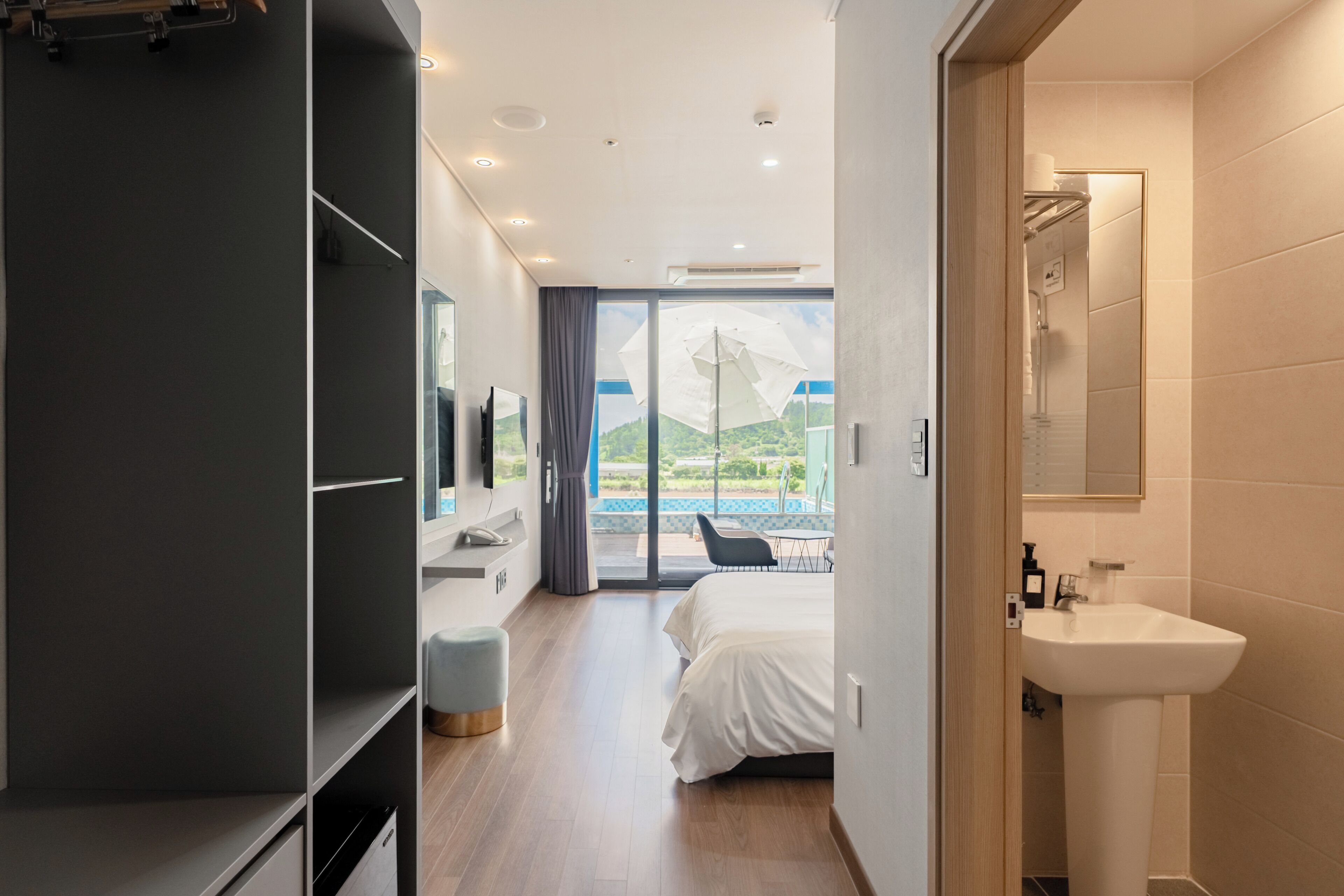 Quarto de hotel moderno com cama, banheiro com pia e vista para uma piscina e montanhas.