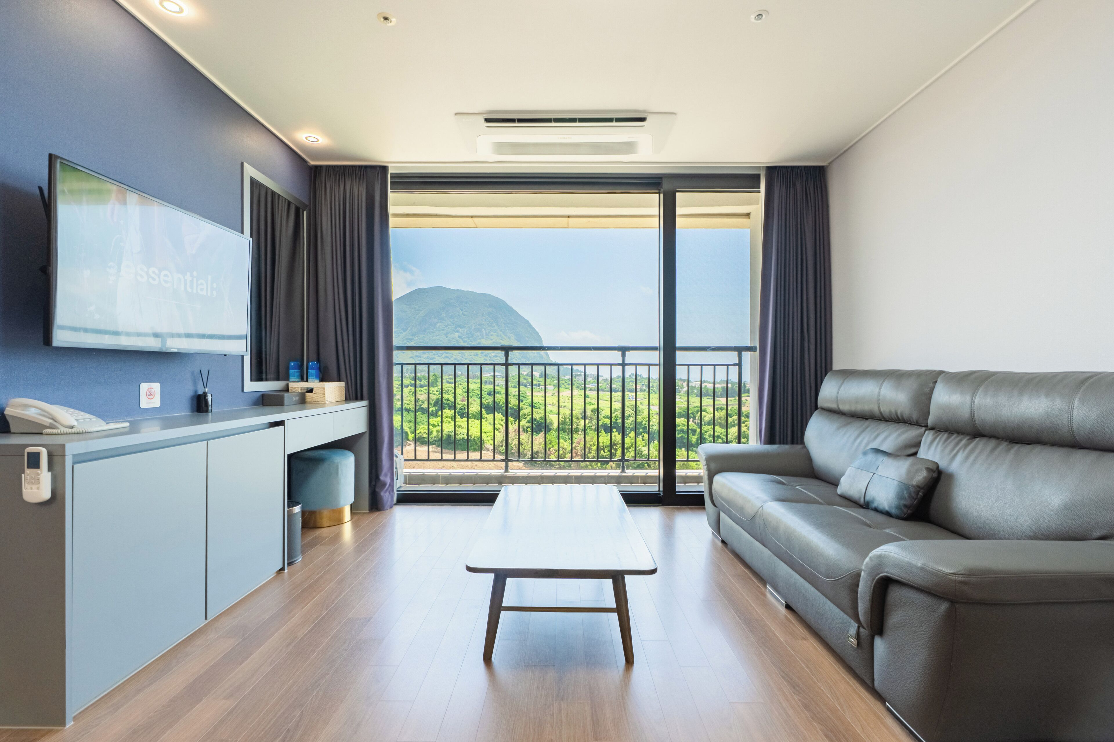 Uma sala de estar moderna com um sofá, uma mesa de centro, uma televisão e uma varanda com vista para o verde e uma montanha.