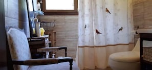 Casa de banho com cadeira de madeira, sanita e cortina de chuveiro com desenhos de aves.