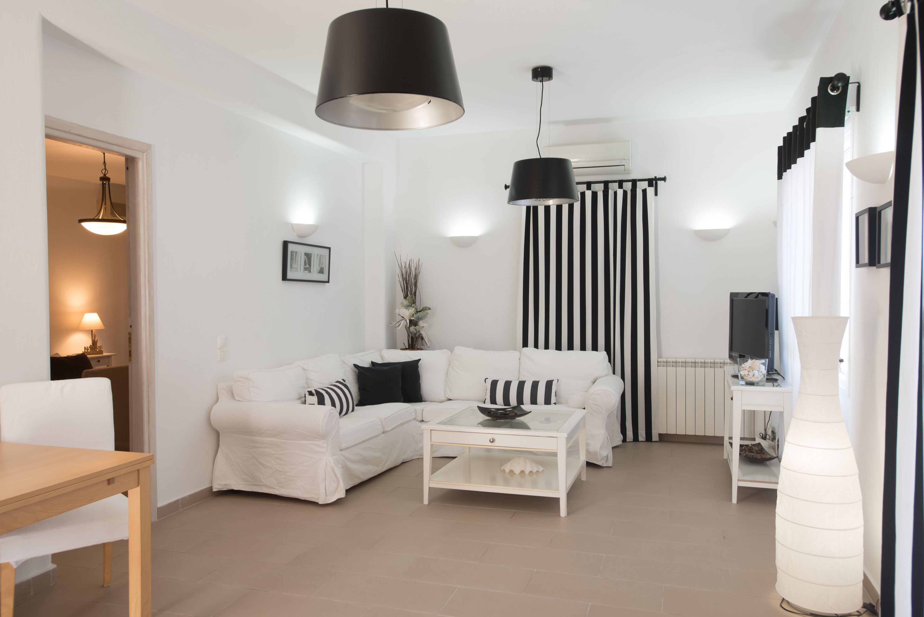 Uma sala de estar moderna com um sofá branco, uma mesa de centro e uma luminária pendente preta.