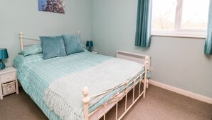 Quarto com cama, mesa de cabeceira, abajur, janela com cortinas e um quadro na parede.