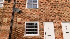 A brick building with two white doors, one labeled "21" and another "23". There are two windows, one with a grid pattern and another with a single pane. A satellite dish is mounted on the wall.