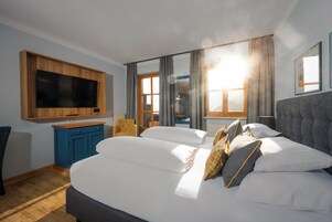 Quarto de hotel com uma cama grande, televisão de tela plana na parede, um armário azul e uma janela com cortinas.