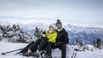 Um casal sentado numa encosta coberta de neve, com montanhas ao fundo.