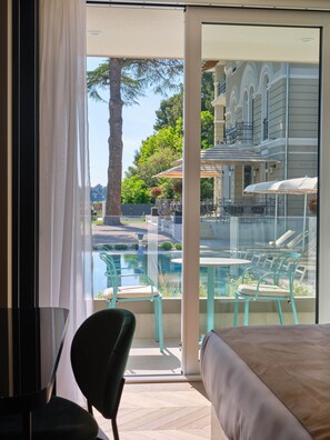 Quarto de hotel com vista para uma piscina, área de estar ao ar livre e um edifício com varandas.