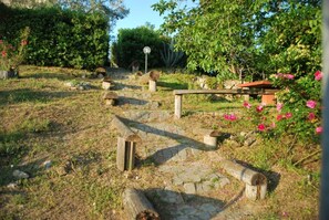 Um caminho de pedra serpenteia subindo uma colina, rodeado por vegetação e flores.