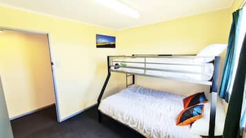 Quarto com beliche, porta, um pequeno quadro e cortina.
