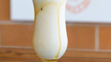 Um copo alto de uma bebida cremosa, com canudo e um raminho de hortelã sobre uma superfície de madeira.
