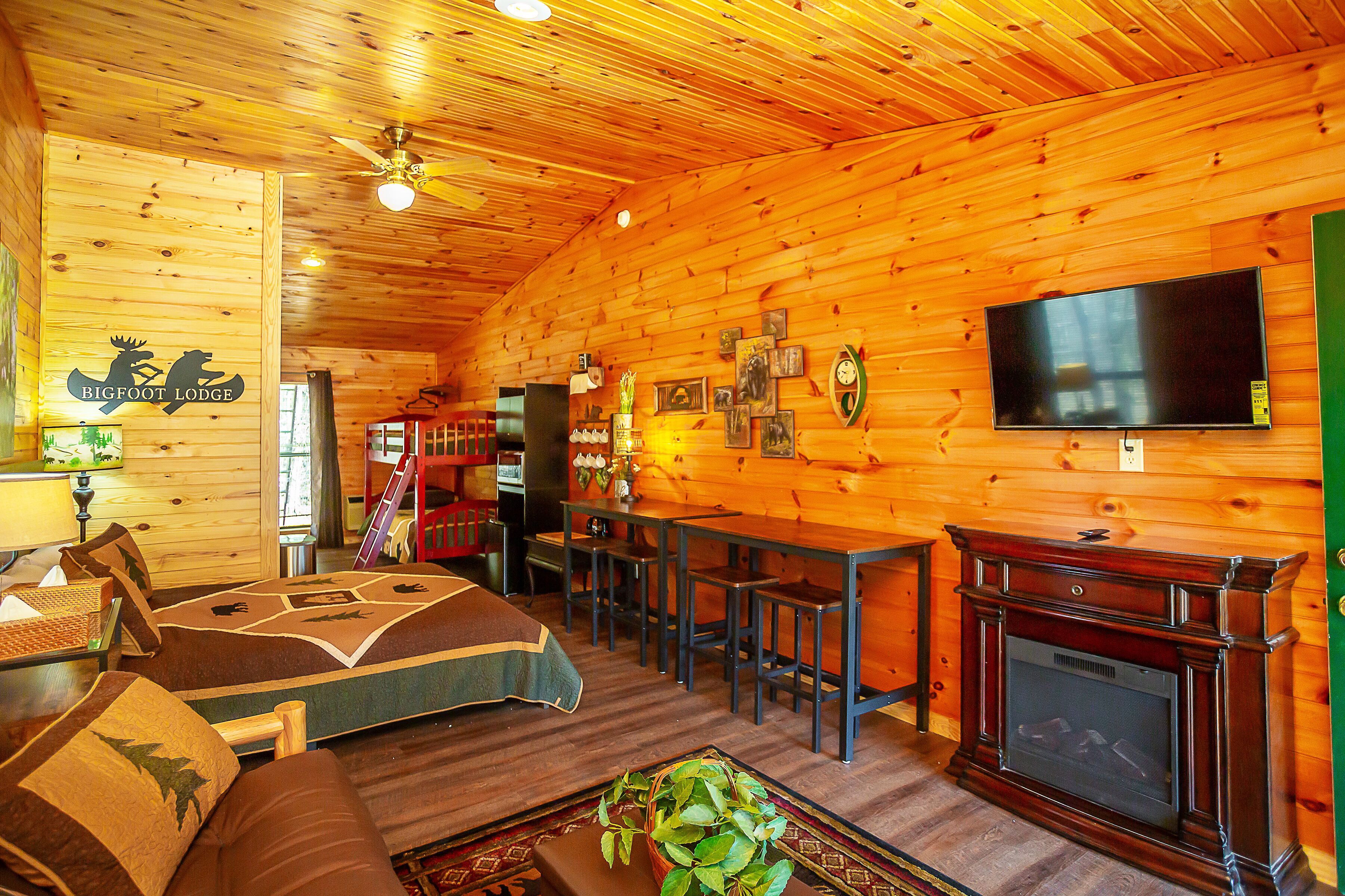 Interior acolhedor de uma cabana com teto de madeira, lareira, televisão e área de jantar.