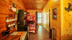 Interior de uma cabana de madeira com cozinha, mesa de jantar e beliche.