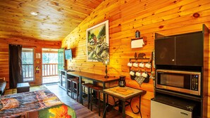 Uma cabana aconchegante com paredes de madeira, área de jantar, cama e cozinha compacta.