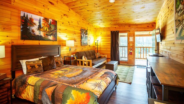 Um quarto de cabana de madeira aconchegante, com uma cama grande, um sofá, uma mesa de jantar e uma pintura de uma paisagem florestal.