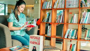 Uma pessoa lendo um livro em um quarto com uma estante repleta de livros.