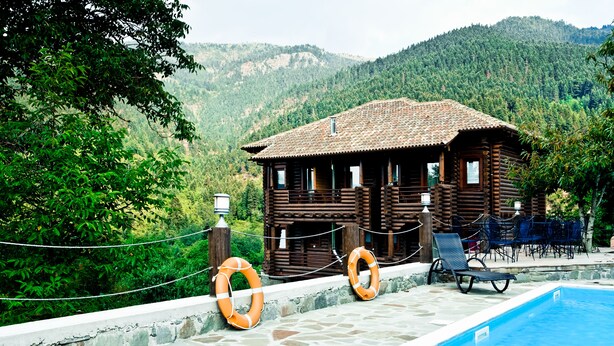Uma cabana de madeira com piscina, rodeada por vegetação exuberante e montanhas.