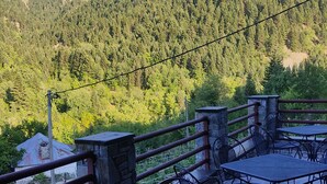 Terraço com área de estar ao ar livre e vista para uma montanha arborizada.