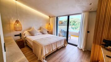 Quarto moderno com uma cama grande, piso de madeira e uma varanda com vista para o verde.