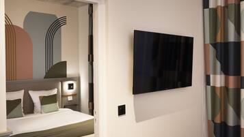 Quarto de hotel com cama, televisão fixada na parede e uma pintura abstrata moderna.