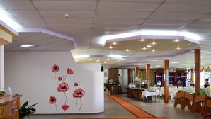 Um saguão de hotel com balcão de recepção, parede com arte floral e área de refeições com mesas e cadeiras.