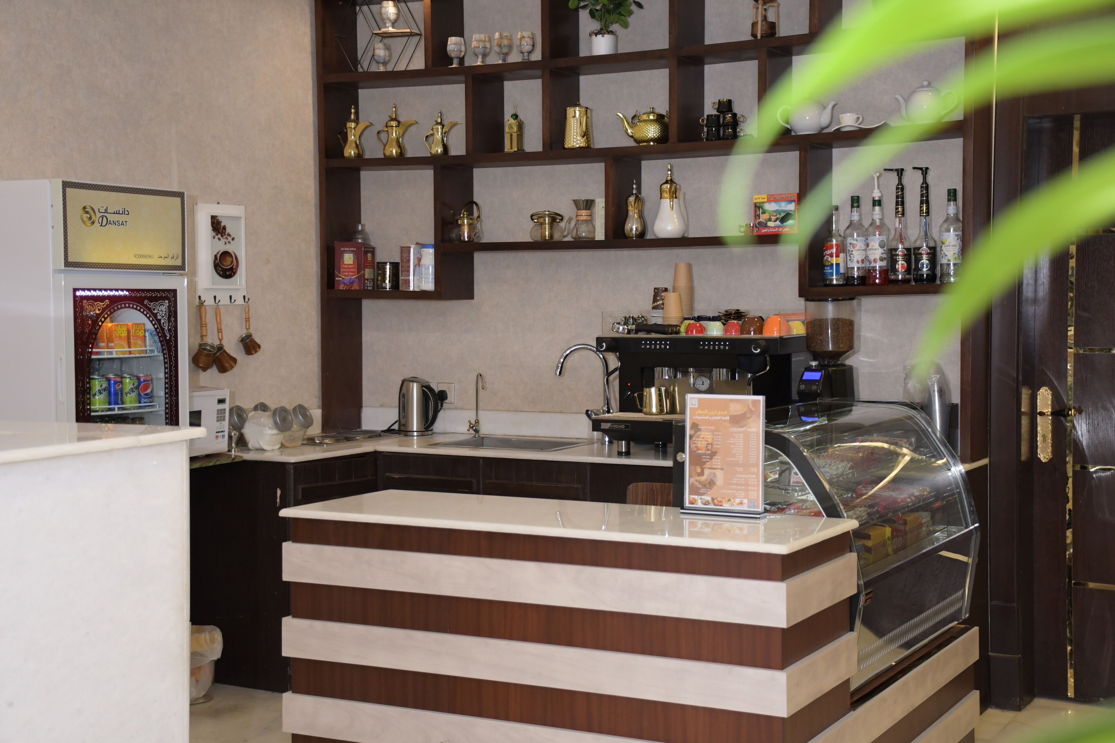 Uma cozinha equipada com cafeteira, geladeira e um expositor com diversos itens.