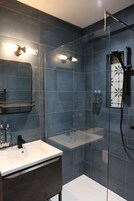 Um banheiro moderno com box de vidro, pia branca e espelho com iluminação embutida.