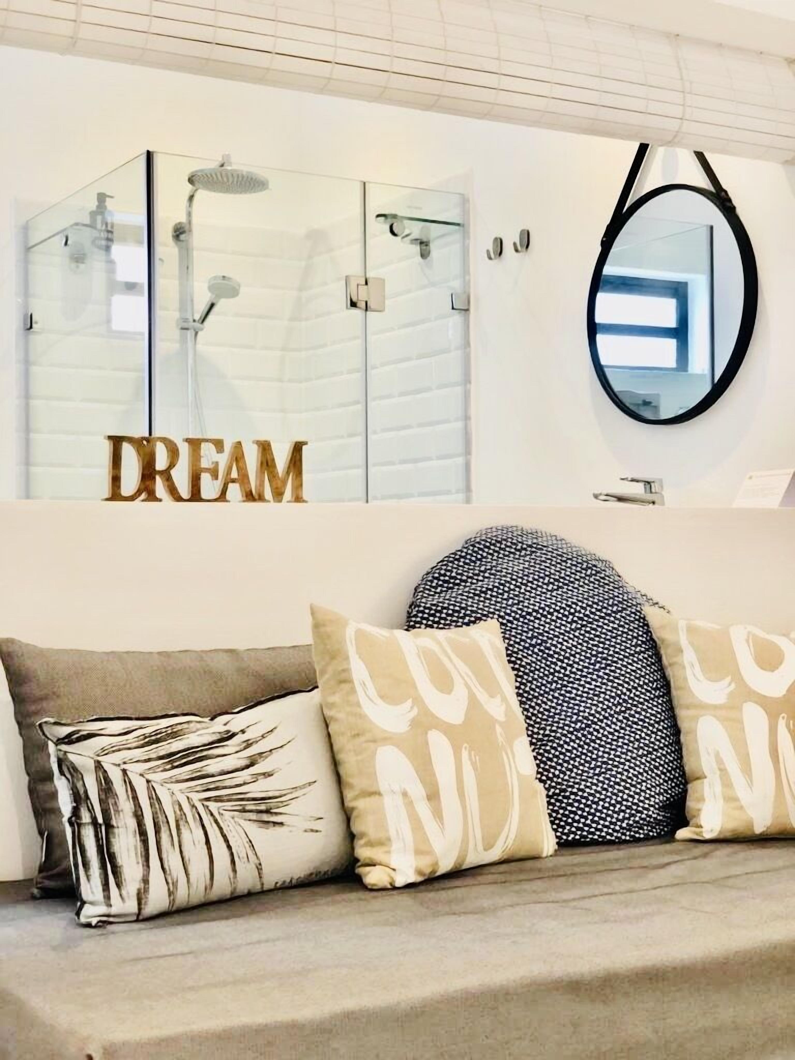 Uma casa de banho moderna com cabine de duche em vidro, espelho redondo e uma placa com a palavra 'DREAM' sobre a pia.