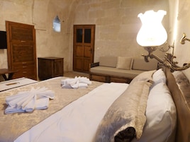 Quarto de hotel com uma cama, um banco de madeira, uma mesinha e uma luminária fixada na parede.
