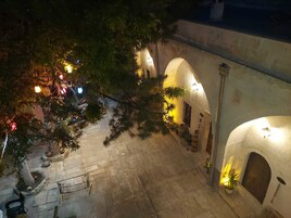 Um pátio externo com piso de pedra, vasos de plantas e arcos iluminados.