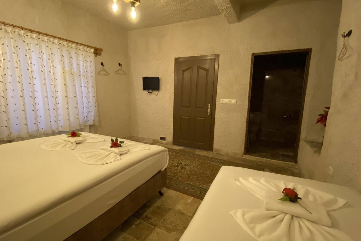 Quarto de hotel com duas camas, uma porta, janela com cortinas e televisão fixada na parede.