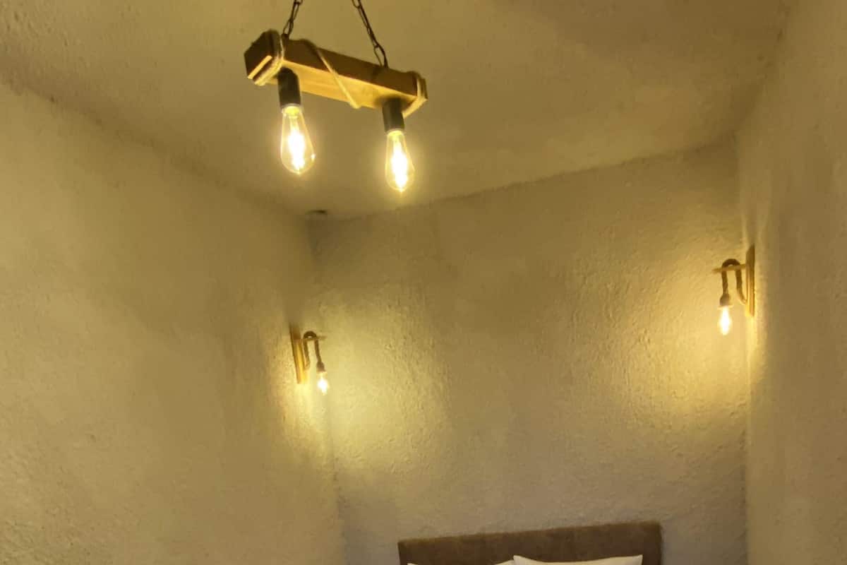 Um quarto pequeno e acolhedor com uma cama de solteiro, uma toalha decorativa na cama e um lustre pendurado acima.