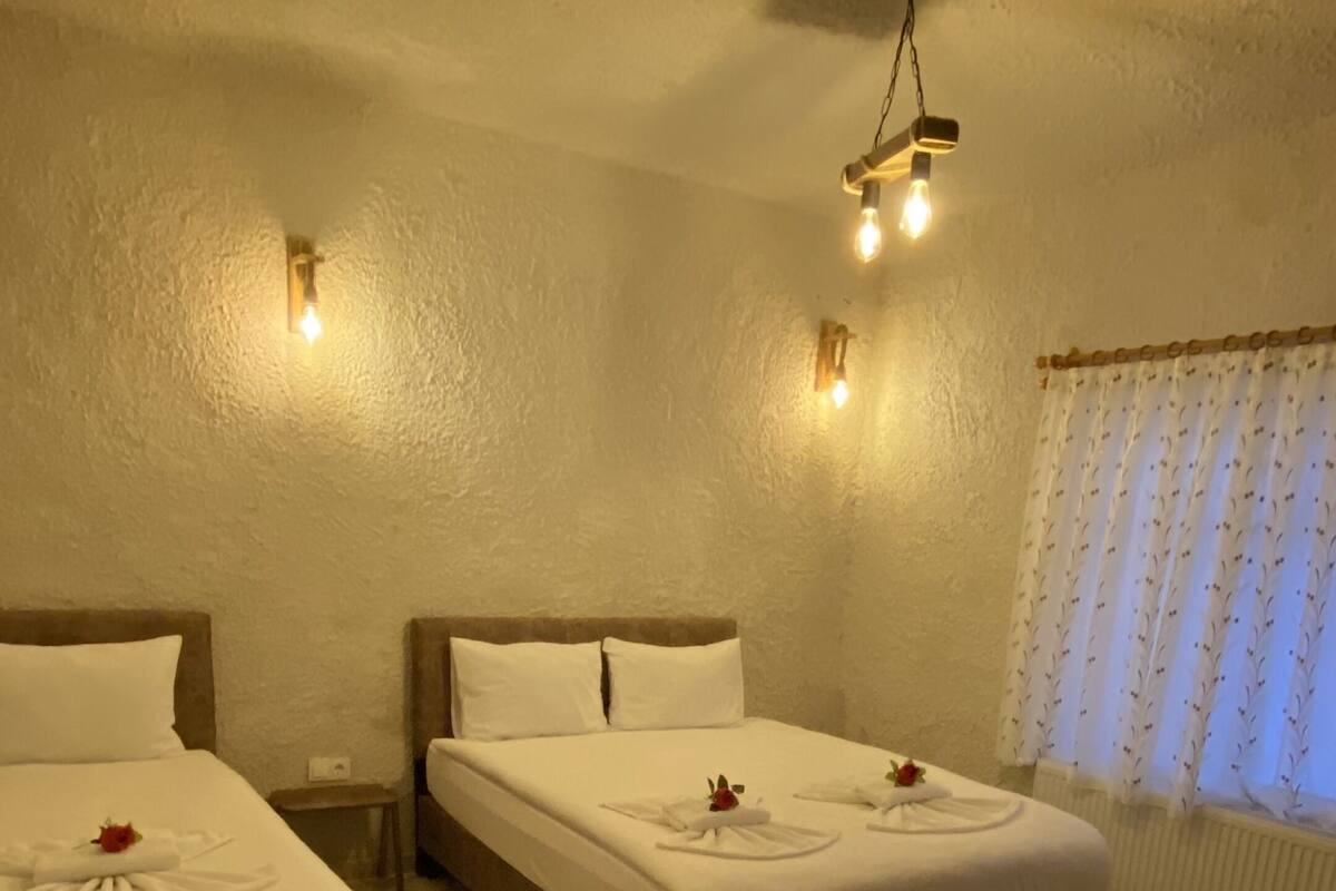 Quarto de hotel com duas camas, um tapete grande estampado, um lustre e uma janela com cortinas.