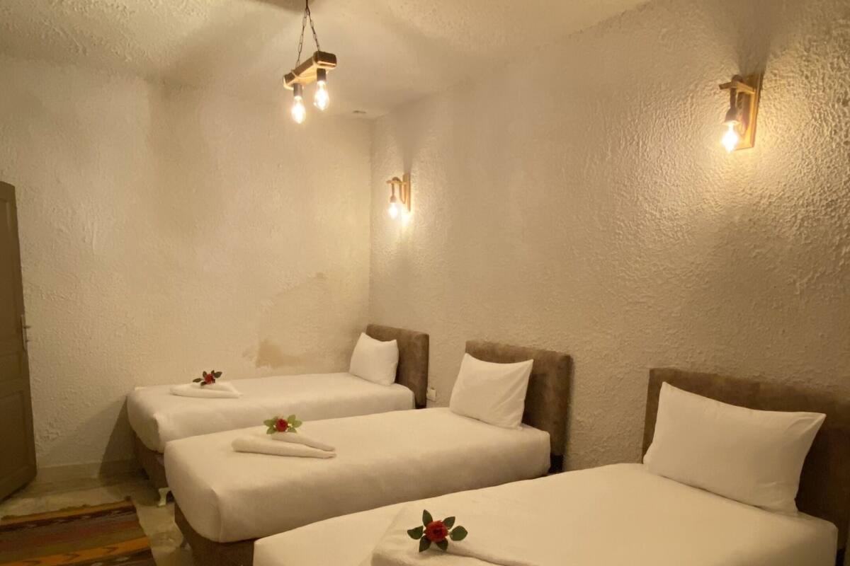 Quarto de hotel com três camas, um tapete estampado e um lustre no teto.