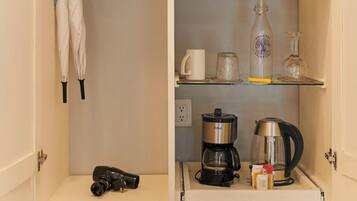Armário bem organizado com prateleiras contendo roupas dobradas, uma cafeteira, uma chaleira e um secador de cabelo.