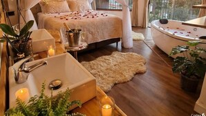 Um quarto luxuoso com uma cama grande, hidromassagem, vista para o exterior e uma área de estar aconchegante com velas.