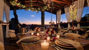 Uma área de refeições ao ar livre com vista para o pôr do sol, decorada com flores e velas.